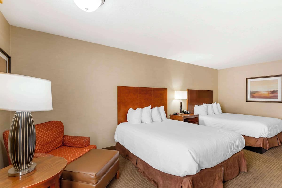 Quarto de hotel com duas camas, um sofá, uma luminária e uma mesa de cabeceira.