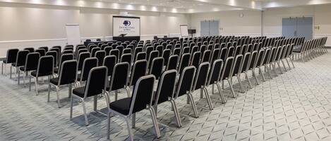 Uma sala de conferências com fileiras de cadeiras, um púlpito e uma tela de projeção.