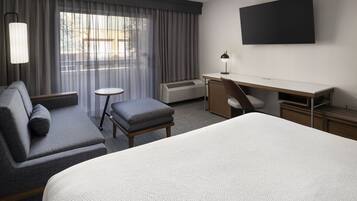 Quarto de hotel com uma cama grande, uma escrivaninha, uma cadeira, uma mesinha e uma televisão.