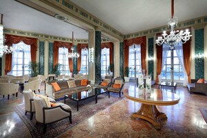 Um amplo hall com piso de mármore, mobiliário elegante e grandes janelas com cortinas.