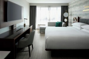 Quarto de hotel com uma cama grande, uma escrivaninha com cadeira, televisão e uma janela com cortinas.