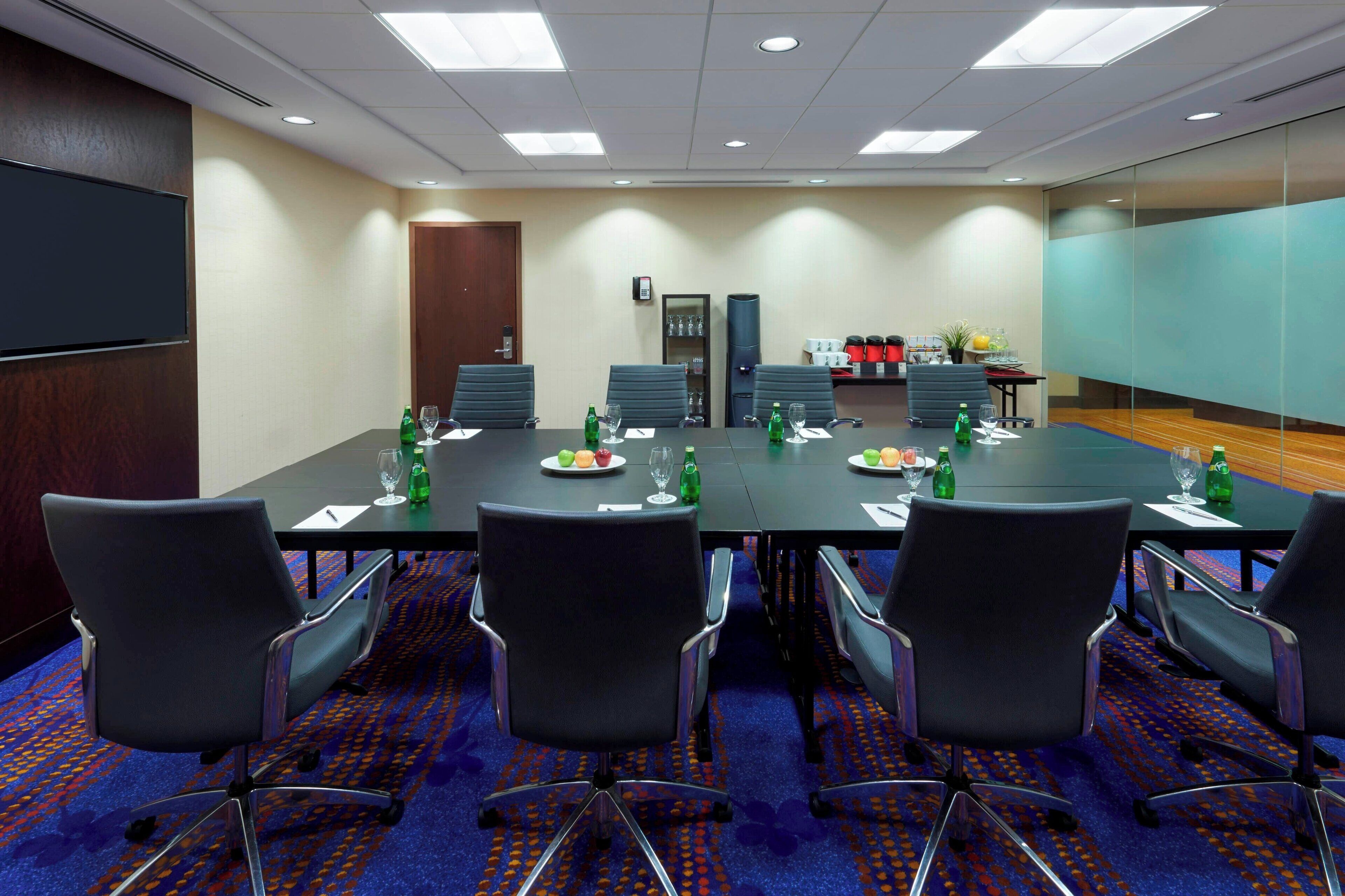 Uma sala de conferências com uma mesa comprida, seis cadeiras e uma tela de projeção.