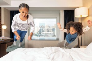 Quarto de hotel com cama, escrivaninha e janela com vista para a cidade.