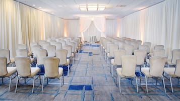 Uma sala de conferências com fileiras de cadeiras, piso coberto de carpete e cortinas de tecido.