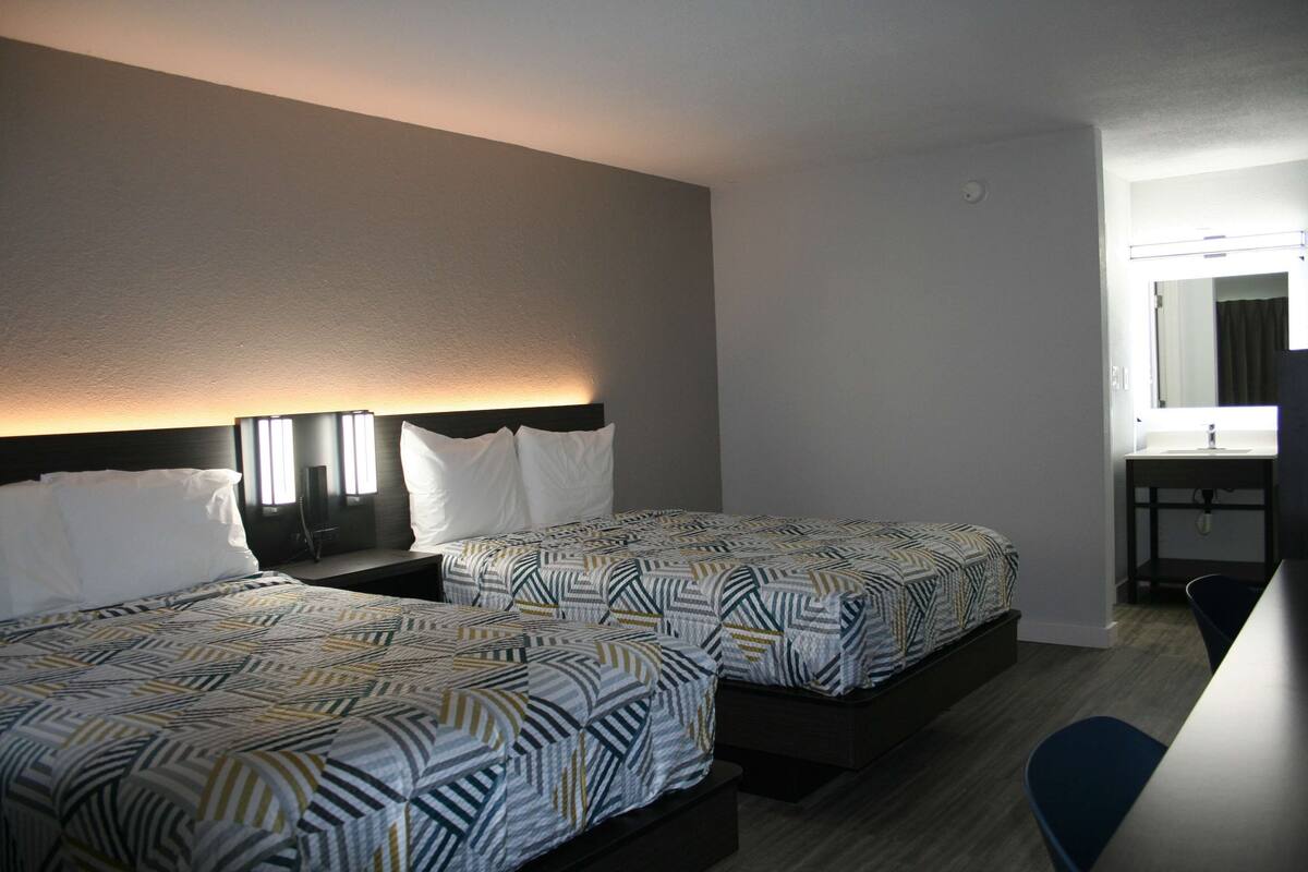 Quarto de hotel com duas camas, uma escrivaninha e um espelho.