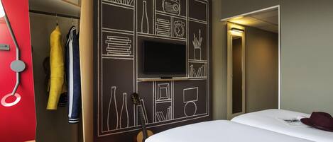 Quarto de hotel com cama, televisão, guarda-roupa e espelho.