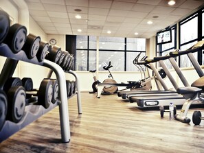Uma academia com equipamentos de ginástica, janelas amplas e um relógio na parede.