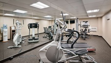 Uma academia com diversos aparelhos de ginástica, um bebedouro e um espelho refletindo os equipamentos.