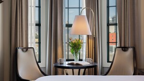 Quarto de hotel com uma cama, duas cadeiras, uma mesa com abajur e um vaso com flores.