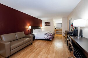 Quarto de hotel com cama, sofá, escrivaninha com luminária, televisão e quadro na parede.