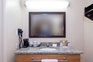Casa de banho com bancada de mármore, lavatório, espelho, telefone e produtos de higiene pessoal.