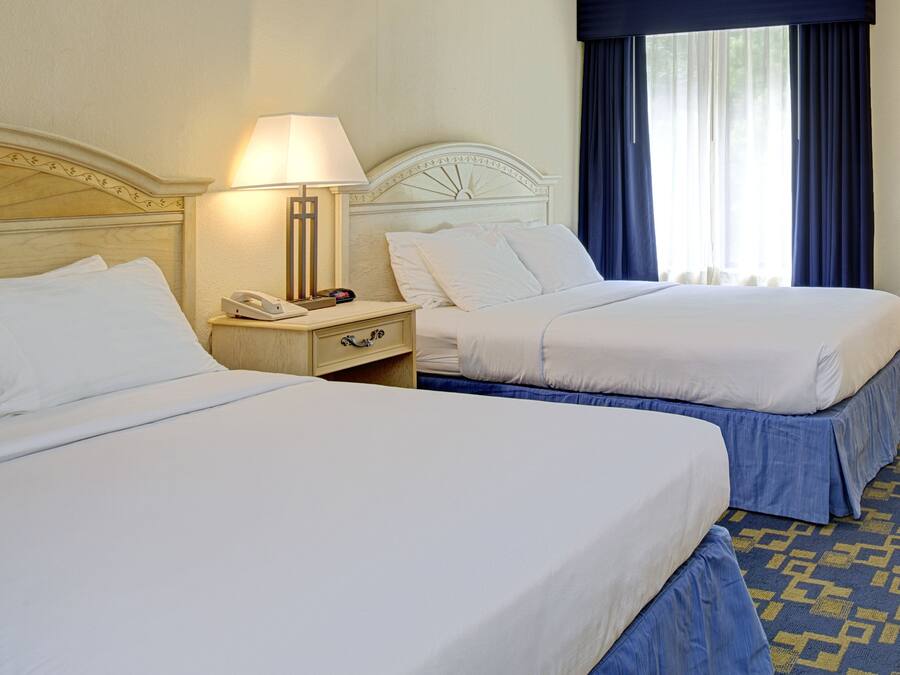 Quarto de hotel com duas camas, uma mesa de cabeceira com abajur e uma janela com cortinas.