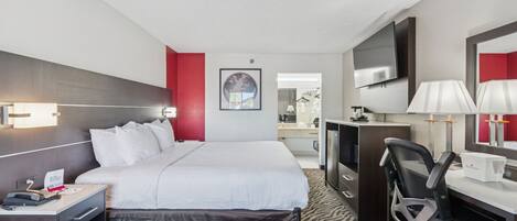 Quarto de hotel com cama, escrivaninha, cadeira, televisão e banheiro visível ao fundo.