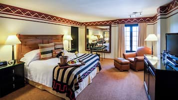 Quarto de hotel com uma cama grande, duas mesas de cabeceira, uma escrivaninha, uma cadeira, uma televisão e uma janela com cortinas.