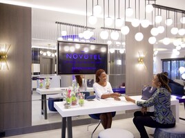 Uma área de recepção de hotel com design moderno, um balcão de atendimento e uma tela grande exibindo o nome e os serviços do hotel.