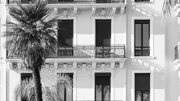 Um edifício com vários andares, varandas, uma palmeira e um restaurante chamado 'RESTAURANT LE DUC' no andar térreo.