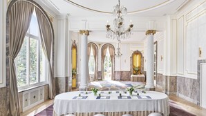 Uma sala de jantar luxuosa com uma mesa redonda posta para refeição, grandes esferas decorativas no chão e um candelabro.