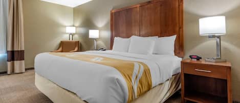 Quarto de hotel com cama, abajures, mesa de cabeceira de madeira e uma janela com cortinas.