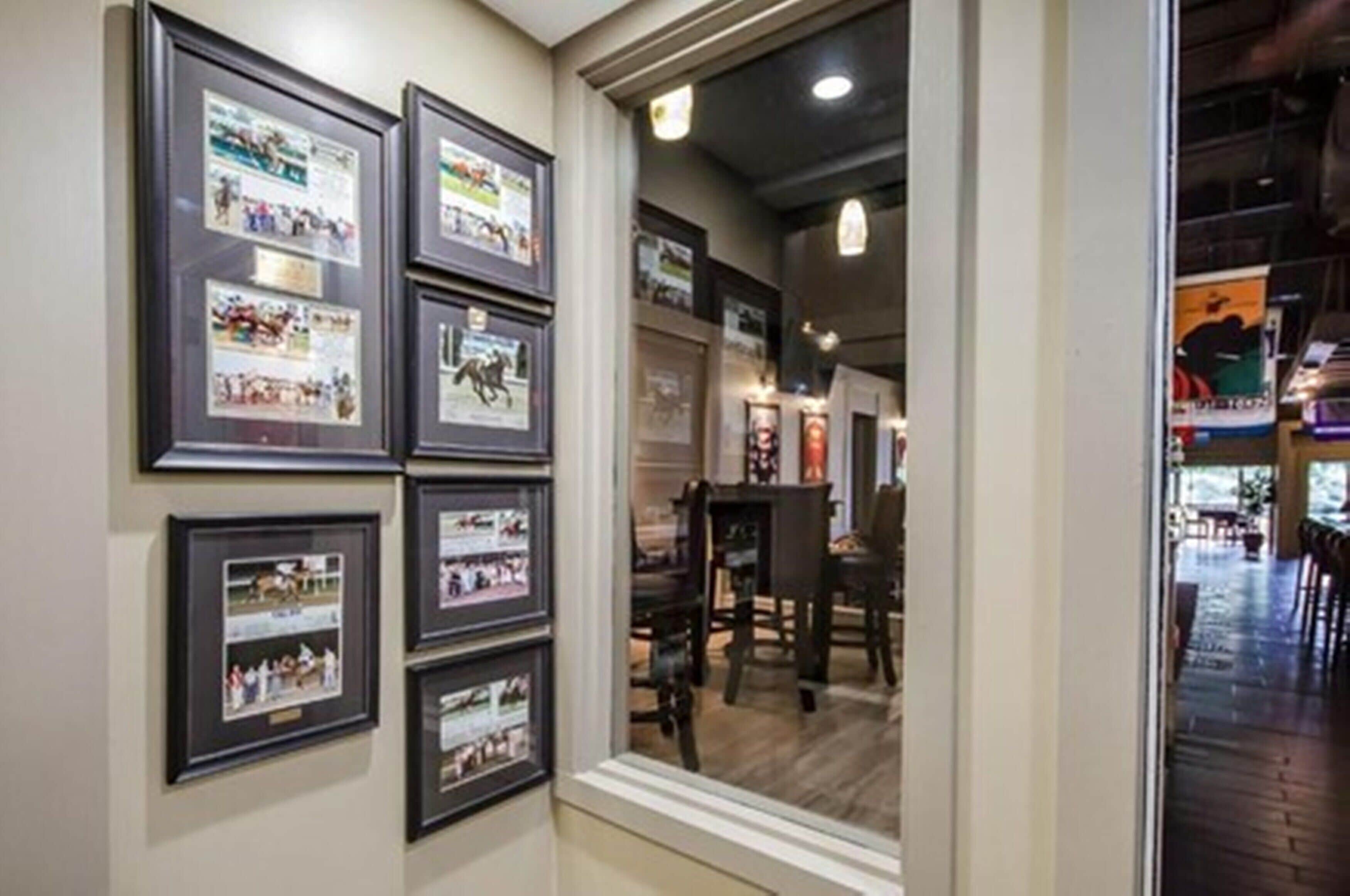 Uma galeria de fotografias emolduradas na parede, uma mesa de madeira com cadeiras e vista para uma sala de jantar.