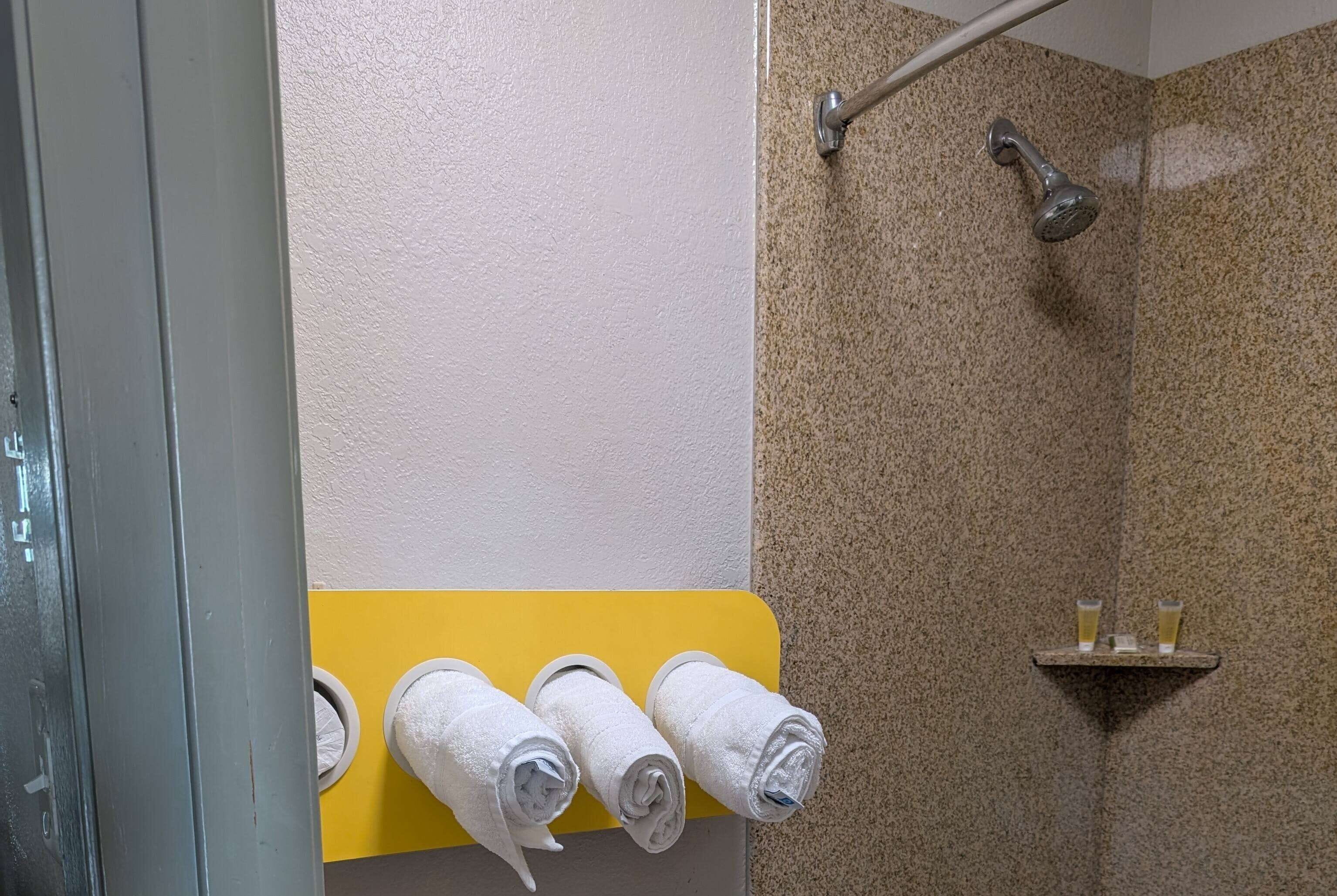 Casa de banho com chuveiro, um porta-toalhas com três toalhas e uma prateleira com dois copos.
