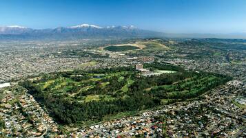 Vista aérea de uma cidade com um grande parque no centro, rodeada por áreas residenciais e montanhas ao fundo.