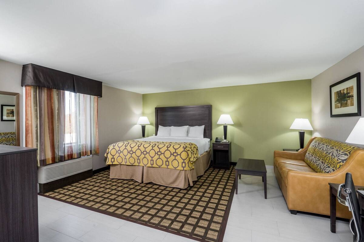 Quarto de hotel com uma cama, duas luminárias de cabeceira, um sofá, uma mesa pequena e uma escrivaninha.