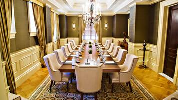 Uma sala de jantar formal com uma longa mesa posta para refeição, rodeada por cadeiras, e um lustre acima.