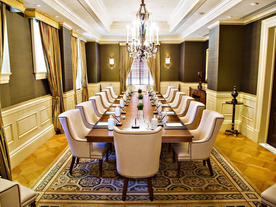 Uma sala de jantar formal com uma longa mesa posta para refeição, rodeada por cadeiras, e um lustre acima.