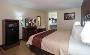 Quarto de hotel com cama, televisão, frigorífico, cómoda, espelho e quadro na parede.