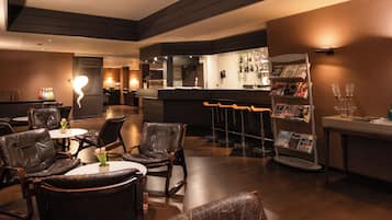 Uma área de bar com cadeiras de couro, balcão com garrafas e revistas.