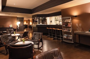 Uma área de bar com cadeiras de couro, balcão com garrafas e revistas.