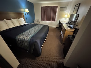 Quarto de hotel com cama, escrivaninha, televisão e janela com cortinas.