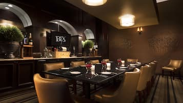 Uma sala de jantar com uma mesa comprida, várias cadeiras e um espaço de bar com televisão e plantas.