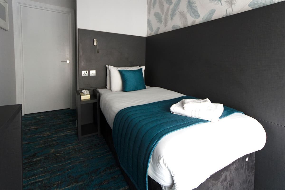 Quarto de hotel com cama, mesa de cabeceira e porta.