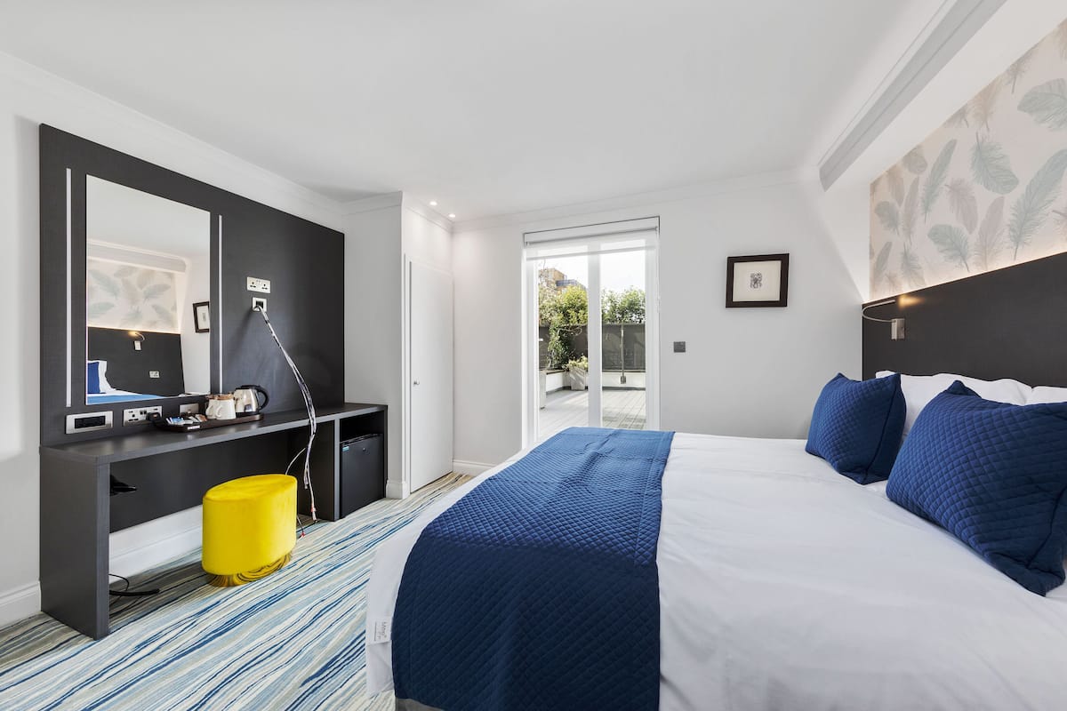 Quarto de hotel moderno com uma cama grande, uma escrivaninha e um banquinho amarelo vibrante.