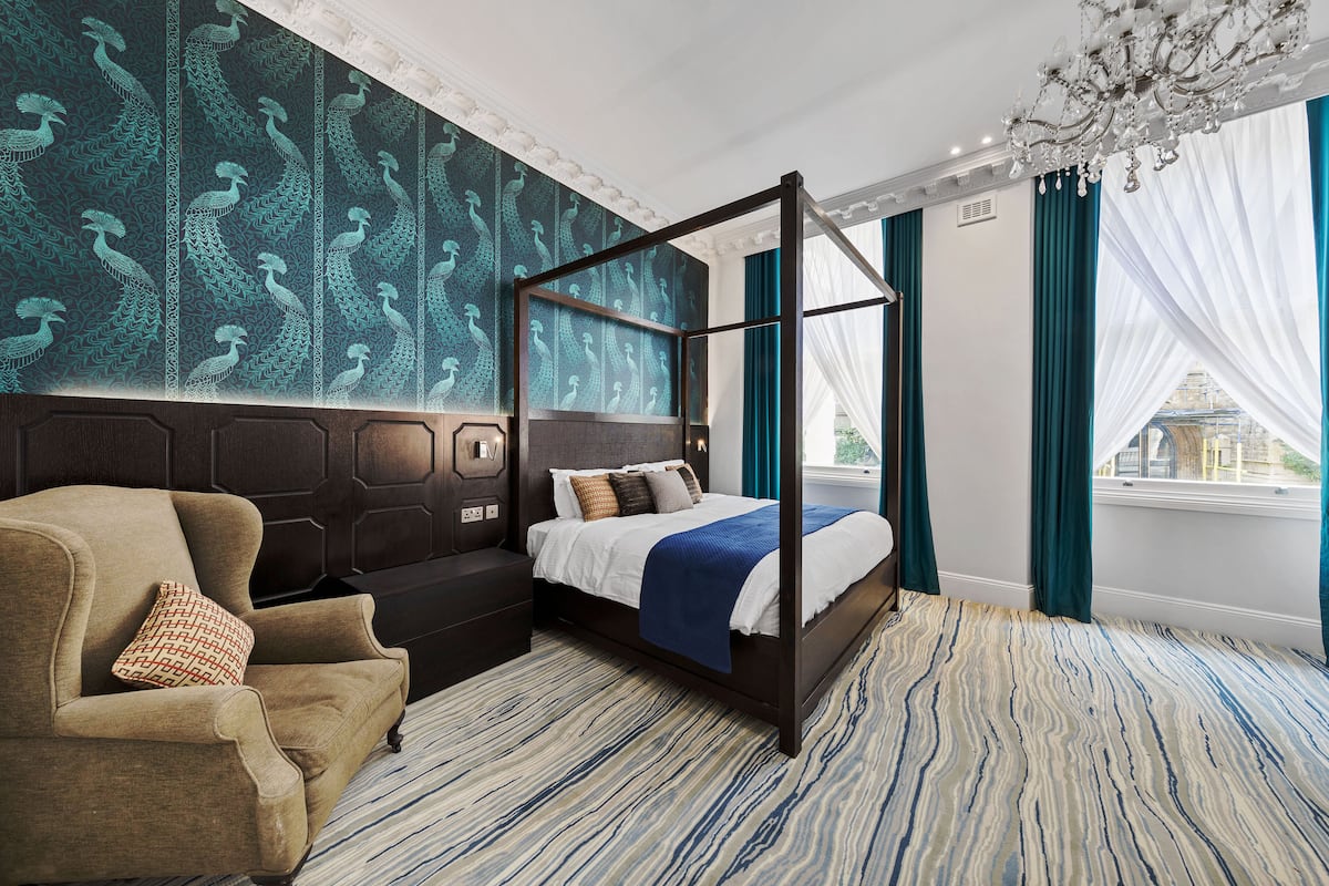 Uma cama de dossel com edredom branco e azul, uma poltrona marrom com almofada estampada e um tapete com padrão.