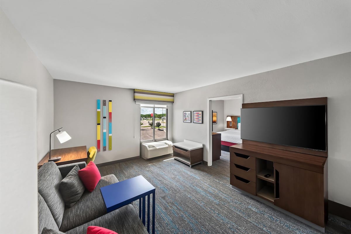 Quarto de hotel moderno com sofá, mesa pequena, televisão, escrivaninha e janela com vista.