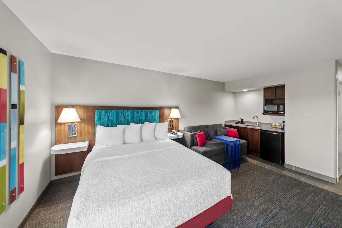 Quarto de hotel com uma cama grande, uma kitchenette pequena, um sofá e uma escrivaninha.