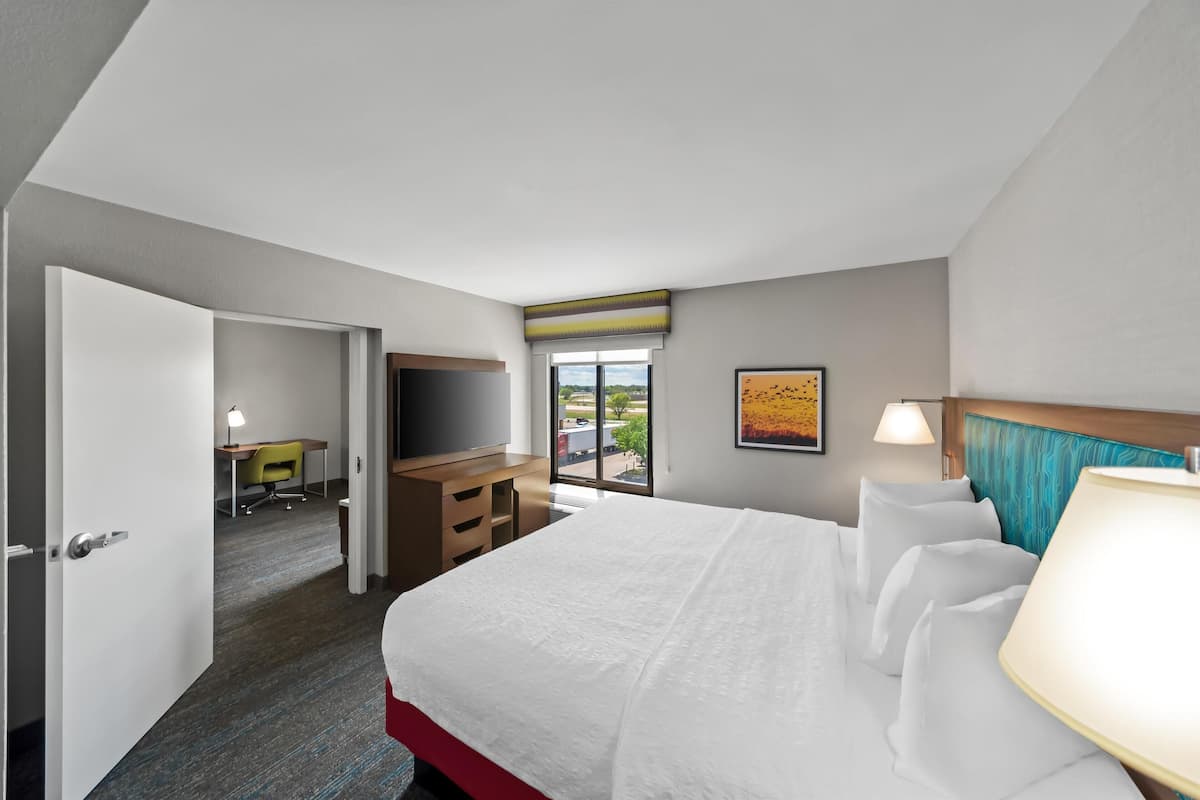 Quarto de hotel com uma cama grande, uma escrivaninha com cadeira, uma televisão e uma janela com vista.