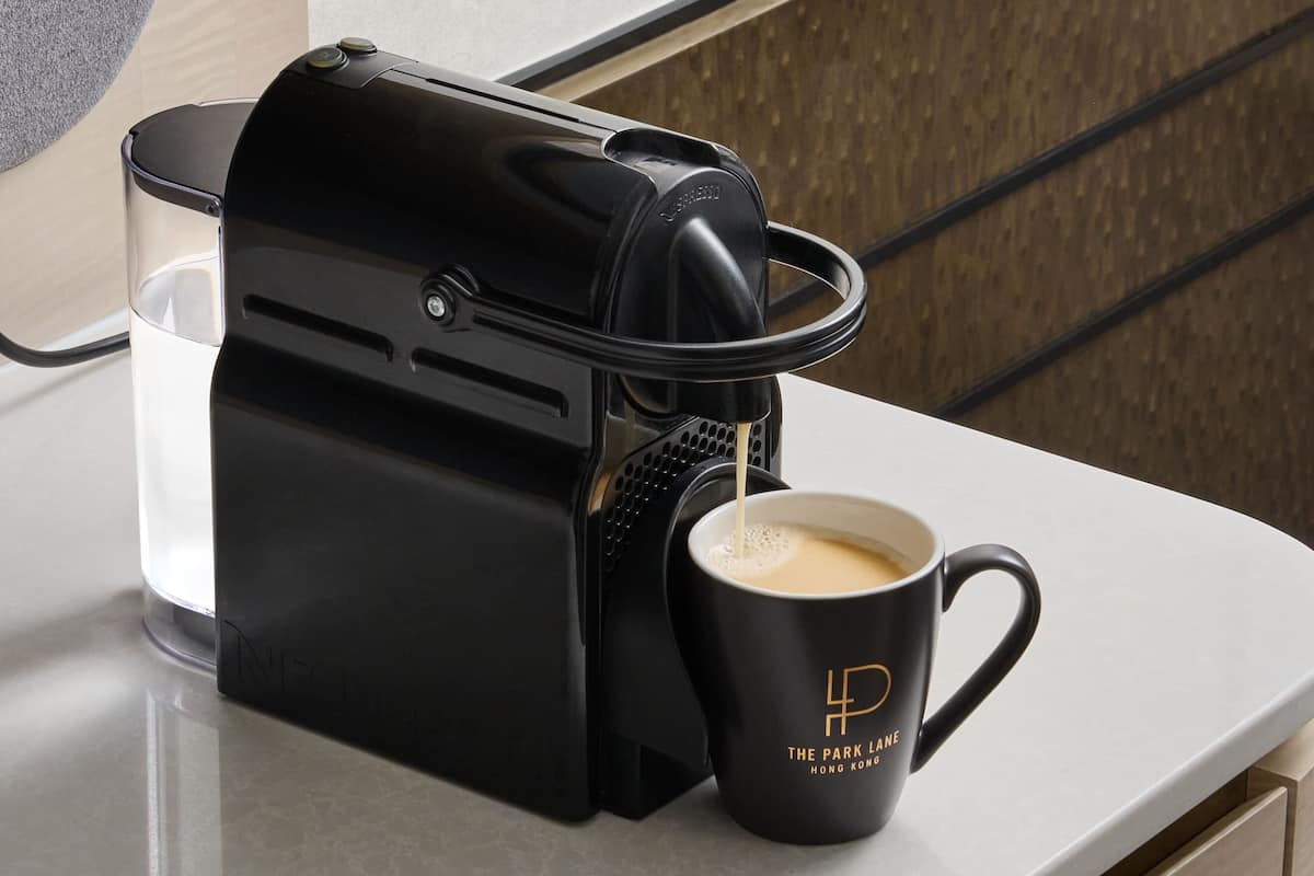 Uma máquina de café numa bancada da cozinha, com uma chávena de café e um copo de água.
