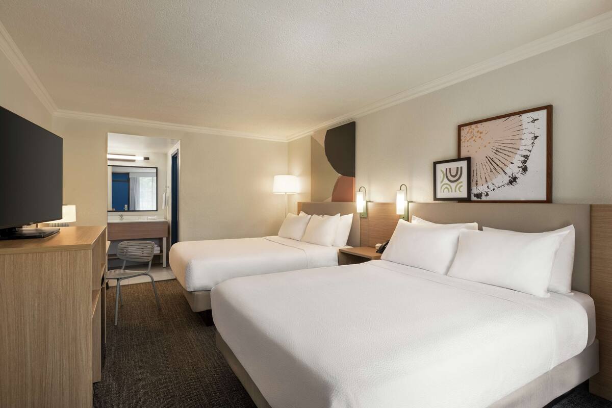 Quarto de hotel com duas camas, uma escrivaninha, uma cadeira e uma televisão.