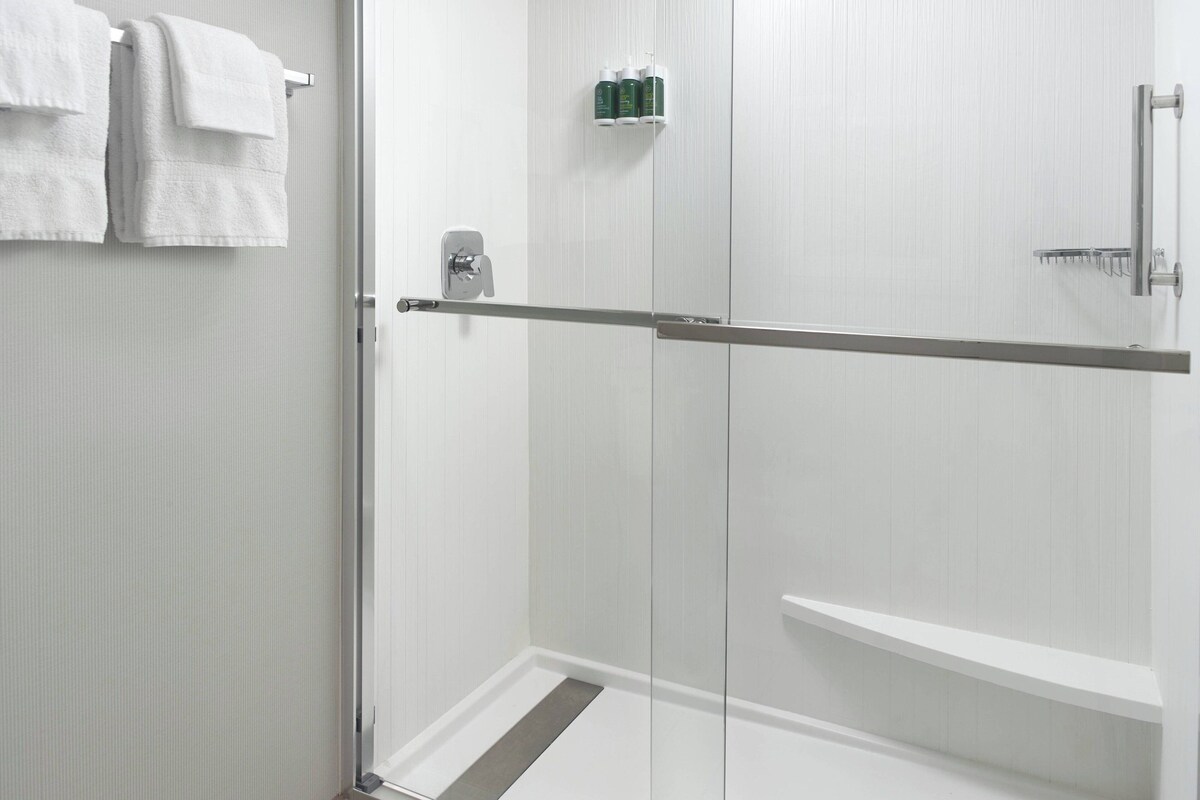 Uma casa de banho moderna com cabine de duche em vidro, um porta-toalhas branco e um prateleira com artigos de higiene pessoal.