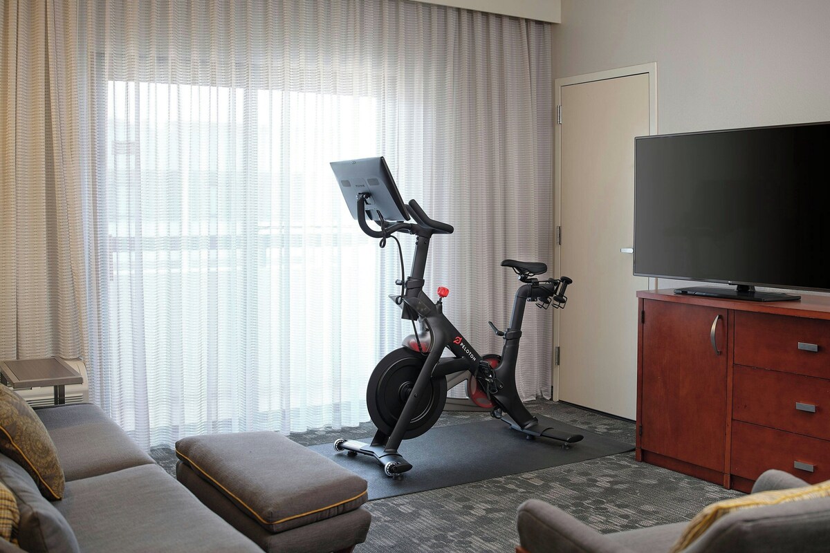 Quarto com bicicleta ergométrica, televisão e sofá.
