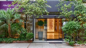 Entrada de hotel moderna com fachada de vidro, ambiente acolhedor e vegetação exuberante ao redor.