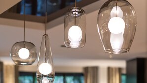 Um interior moderno com luminárias pendentes, uma área de refeições com cadeiras vermelhas e grandes janelas que oferecem vista para o verde lá fora.