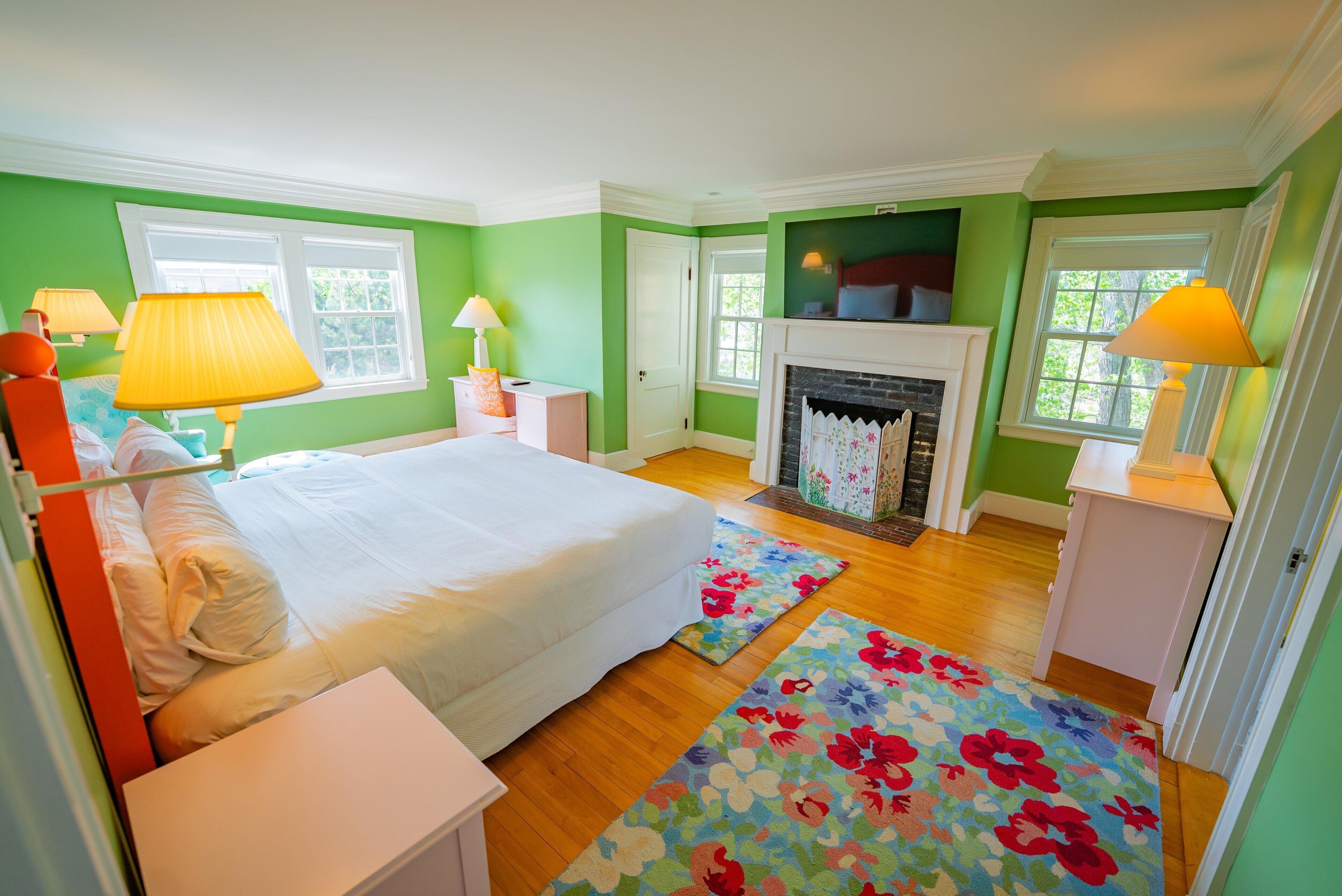 Quarto com cama, luminárias de cabeceira, lareira e tapete floral.