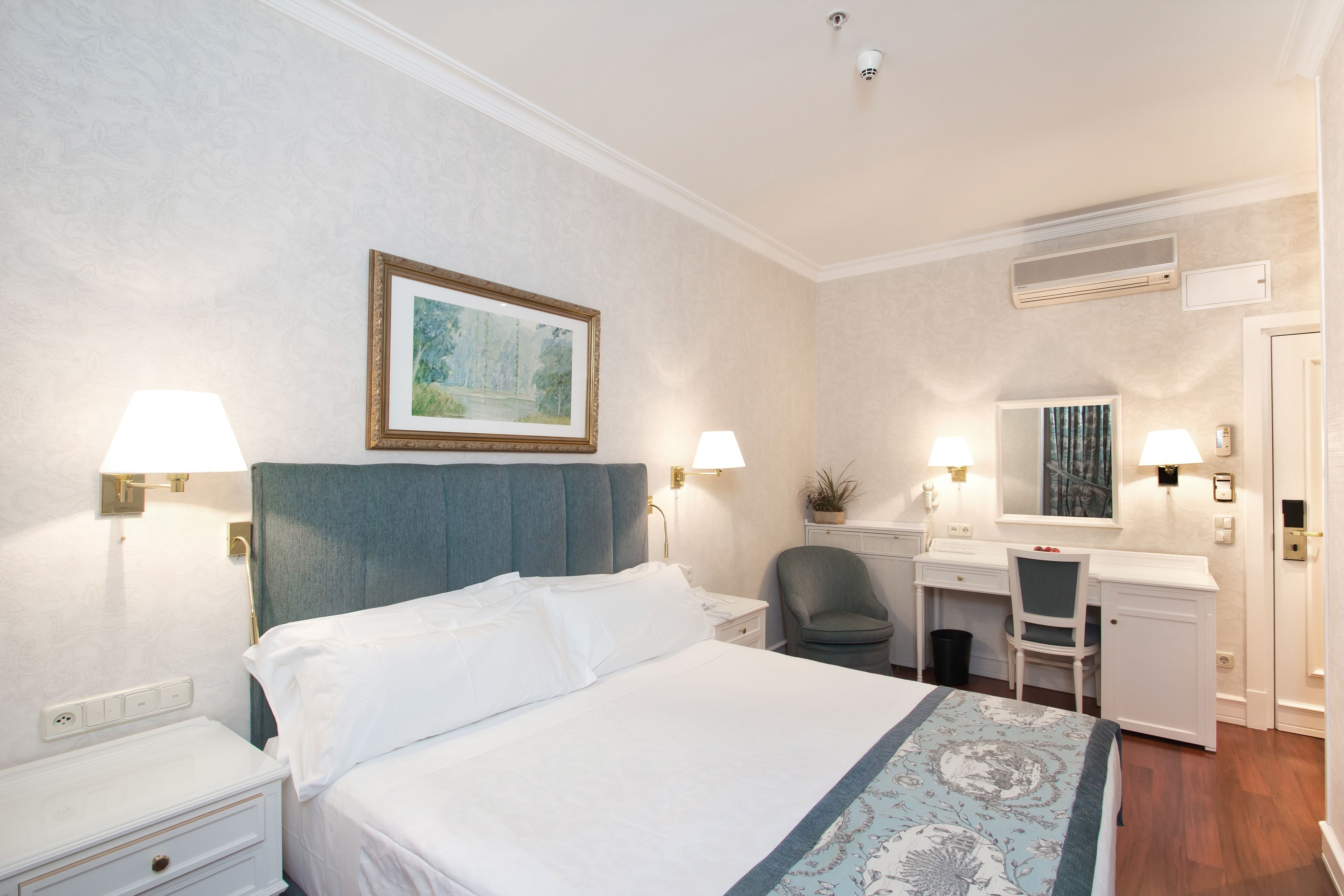 Quarto de hotel com cama, escrivaninha, cadeira e um quadro na parede.