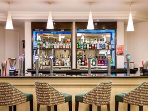 Uma área de bar com vários dosadores de bebidas, uma seleção de garrafas e três banquetas estofadas.