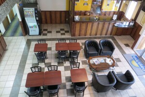 Um café com várias mesas e cadeiras, uma máquina de vendas automática e um balcão com divisória de vidro.