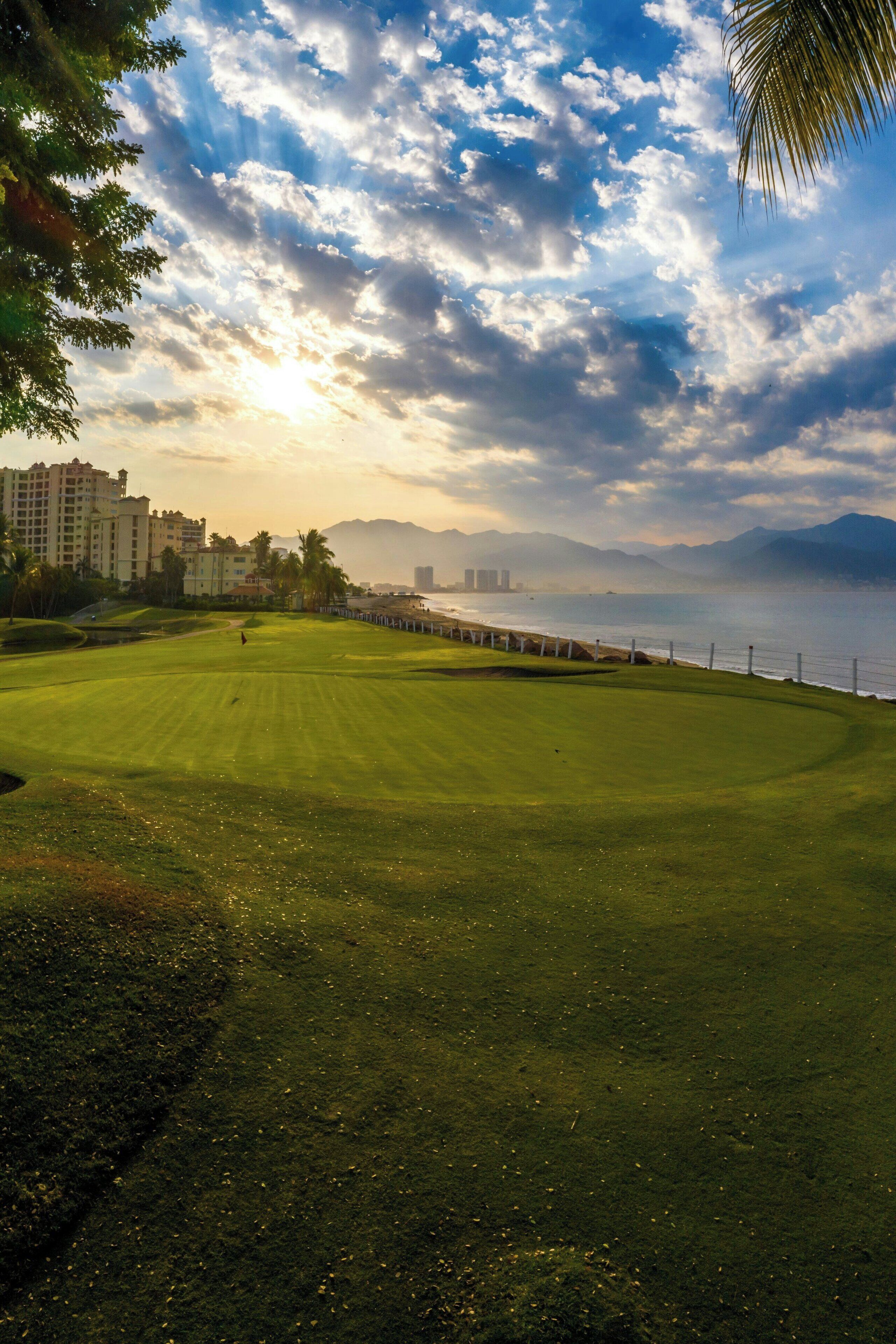 Um campo de golfe com vista para o oceano e montanhas ao fundo.